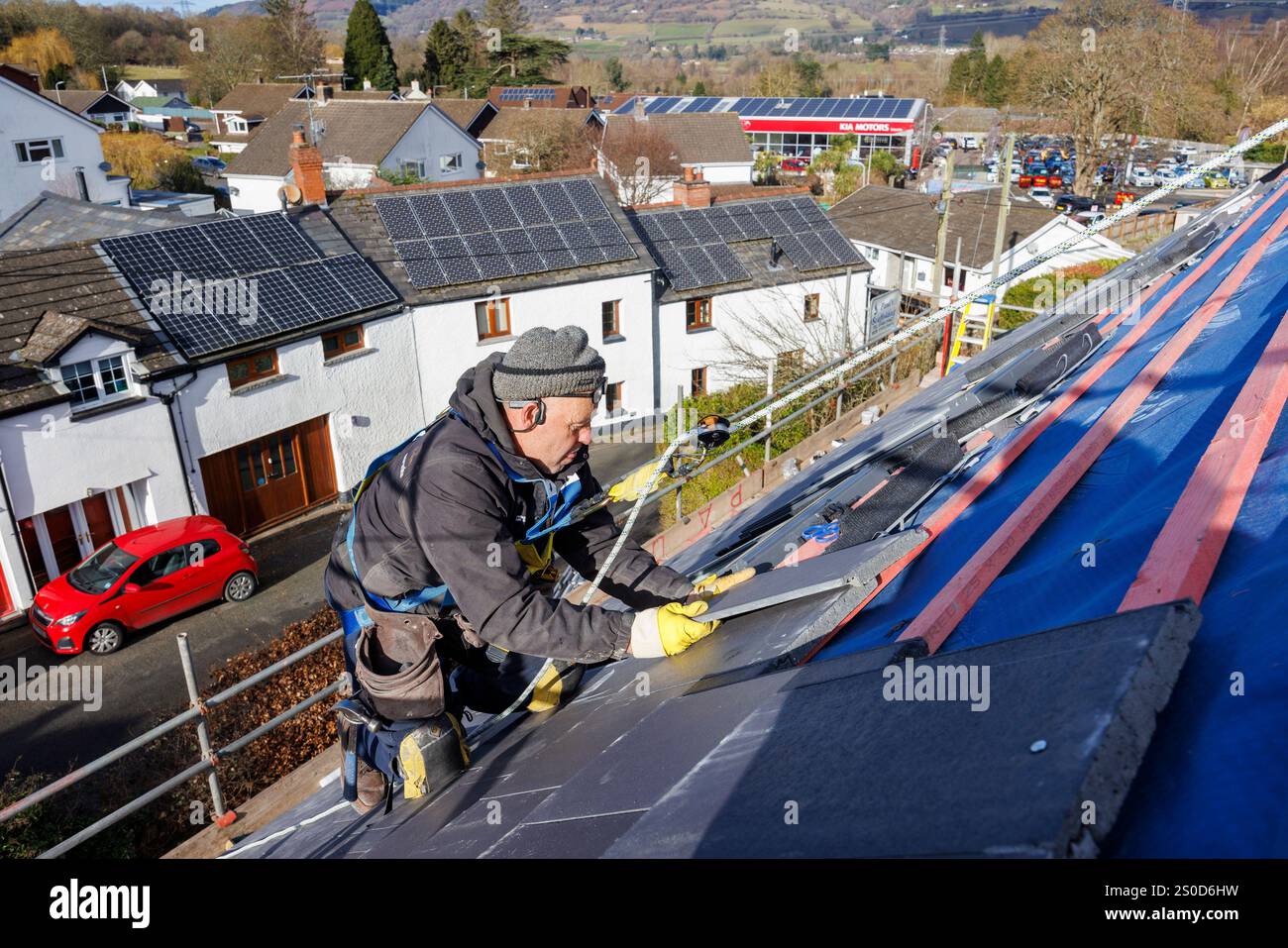 Roofer using safety equipment including rope to replace tiles on house ...