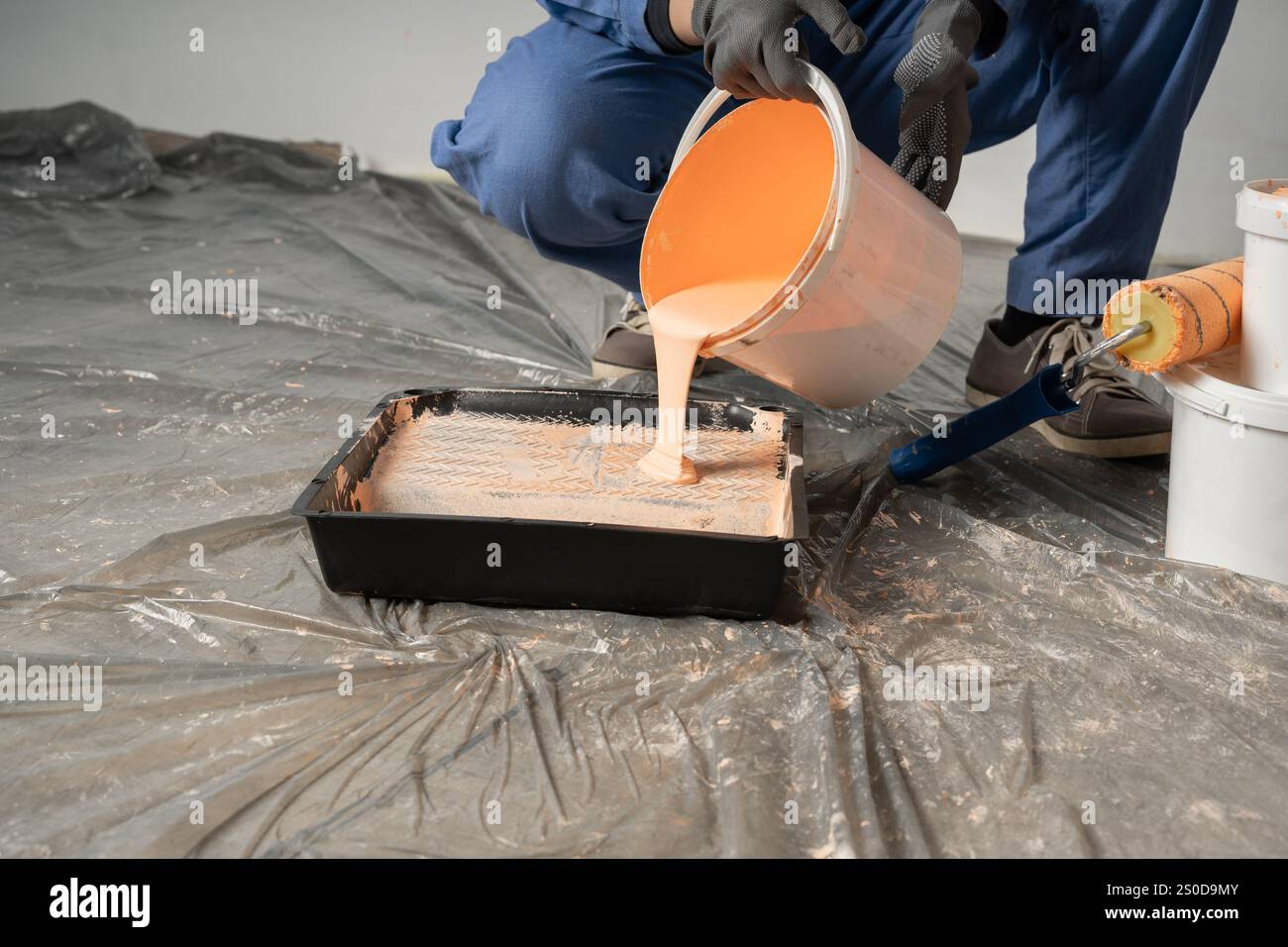 female decorator pours paint into painting tray indoors. Tools for ...