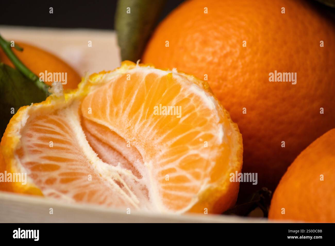 Close up of whole mandarines and one peeled fruit in a wooden box on ...