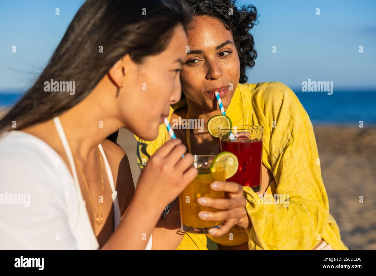 Two young women enjoying refreshing drinks on beach Stock Photo - Alamy