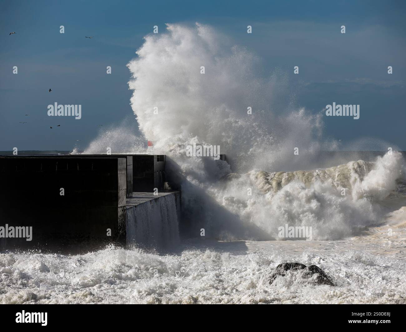 Big white wave against a pier with a beacon from the Douro harbor ...