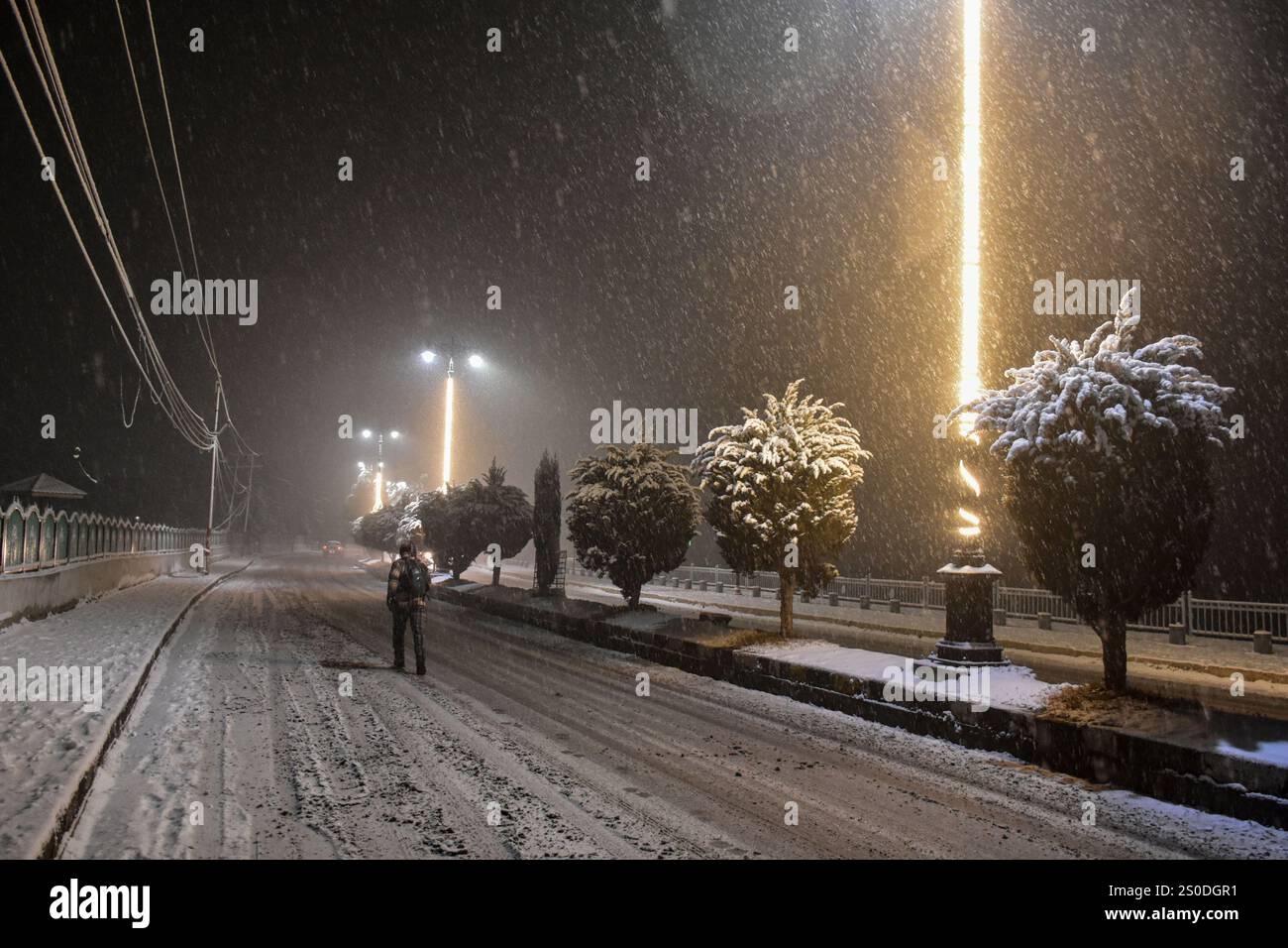 A man walks along the snow covered road during snowfall in Srinagar ...