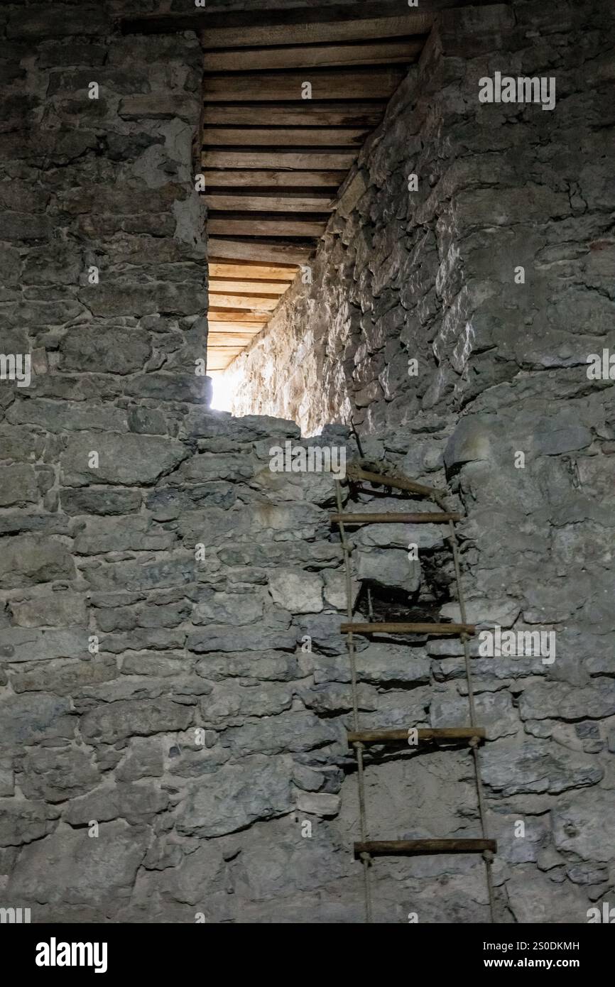 A stone wall with a ladder leading up to it. The ladder is rusted and ...