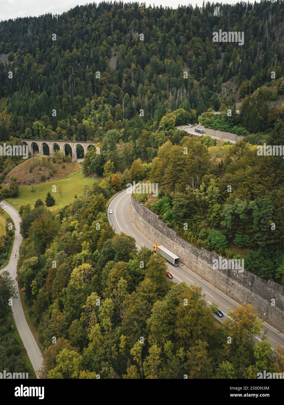 Aerial view of a winding mountain road lined with lush forest and a ...