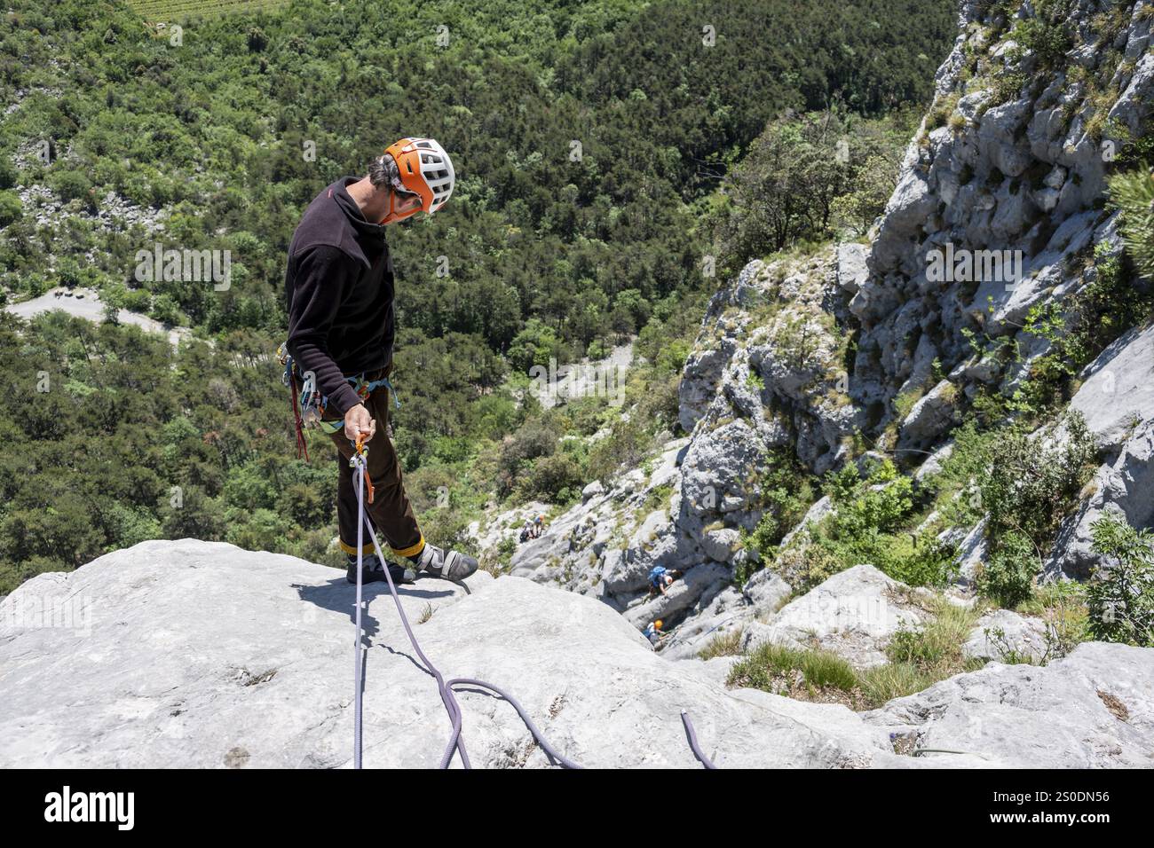 A climber in safety equipment descends a rocky mountain face, alpine ...