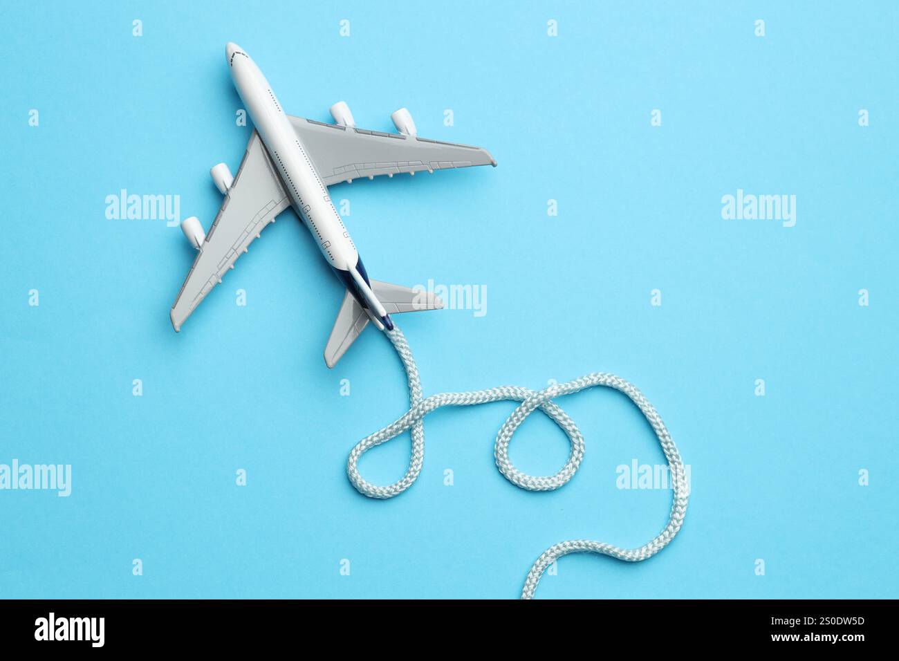 Plane model and rope as flight path on light blue background, top view ...