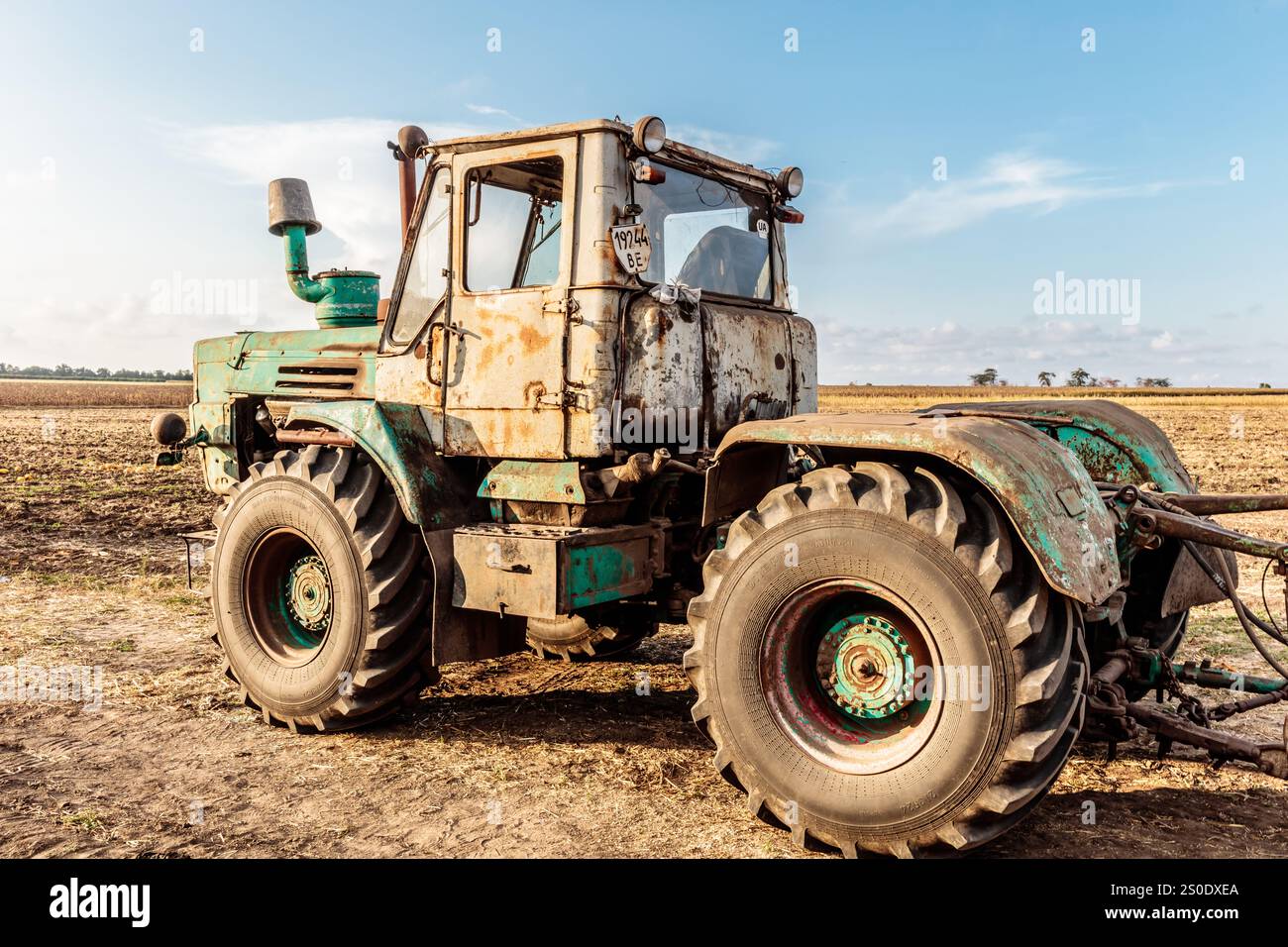 An old green tractor is parked in a field. The tractor is rusty and has ...