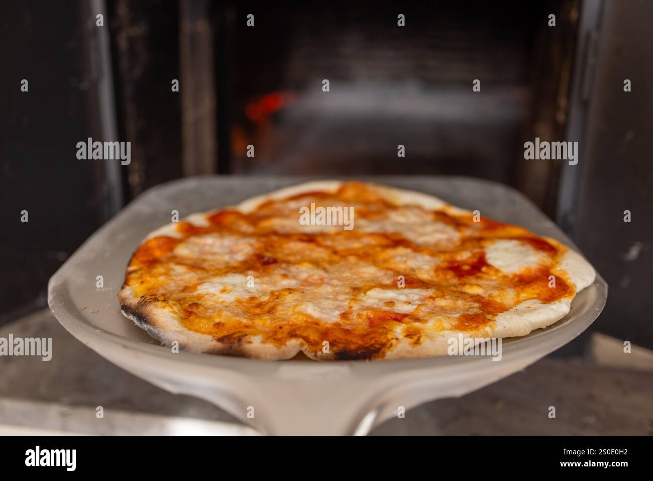 A freshly baked pizza resting on a pizza peel, ready to be served from ...