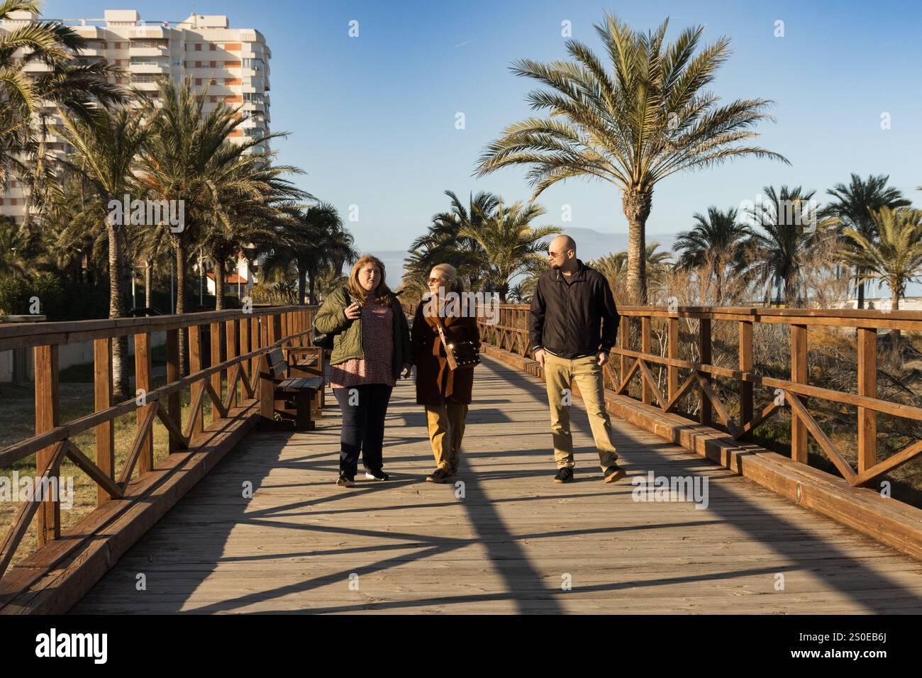 Three people are walking and talking along a scenic wooden boardwalk ...