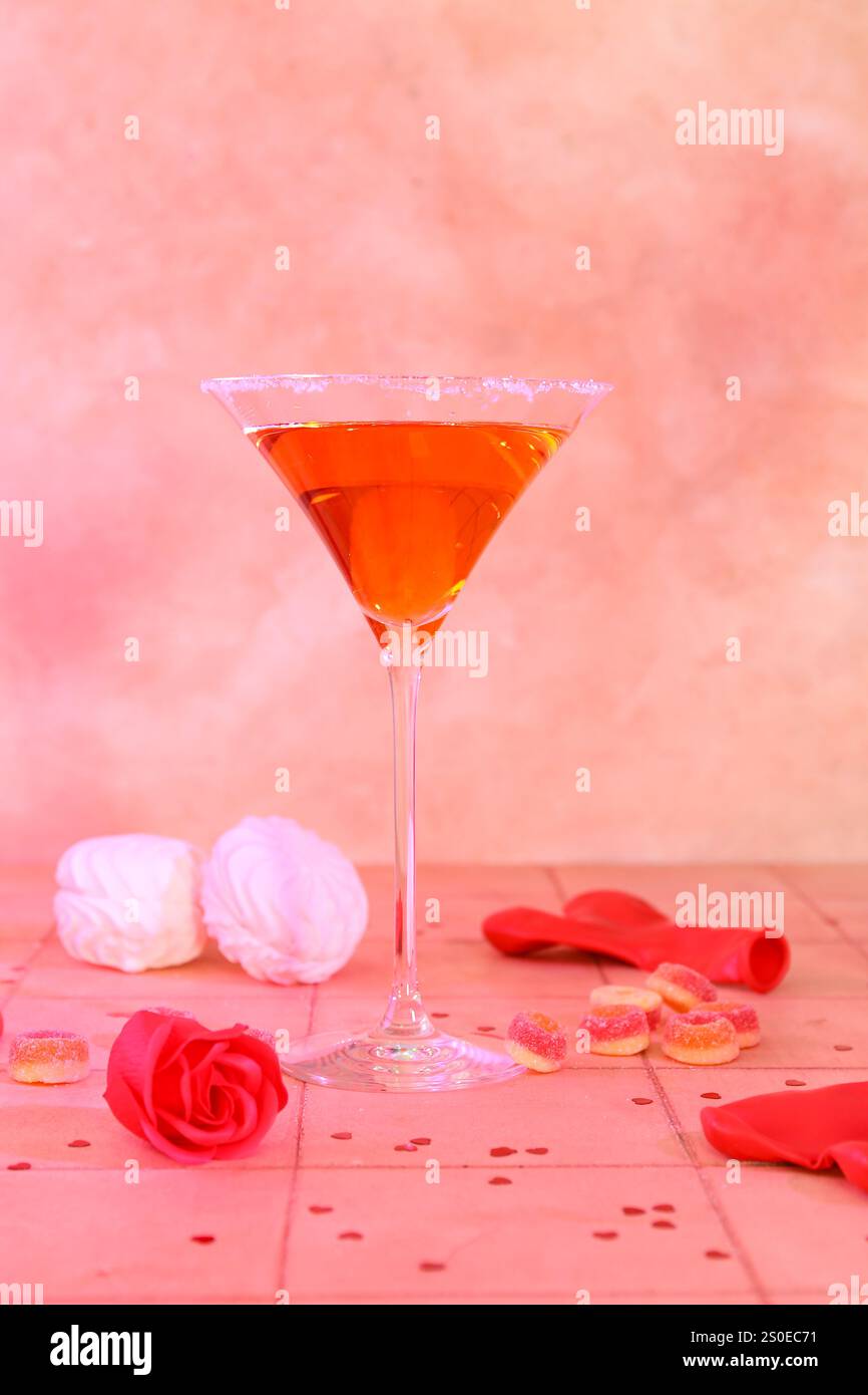 Glass of tasty cocktail with sweets, rose and balloons on tile table ...