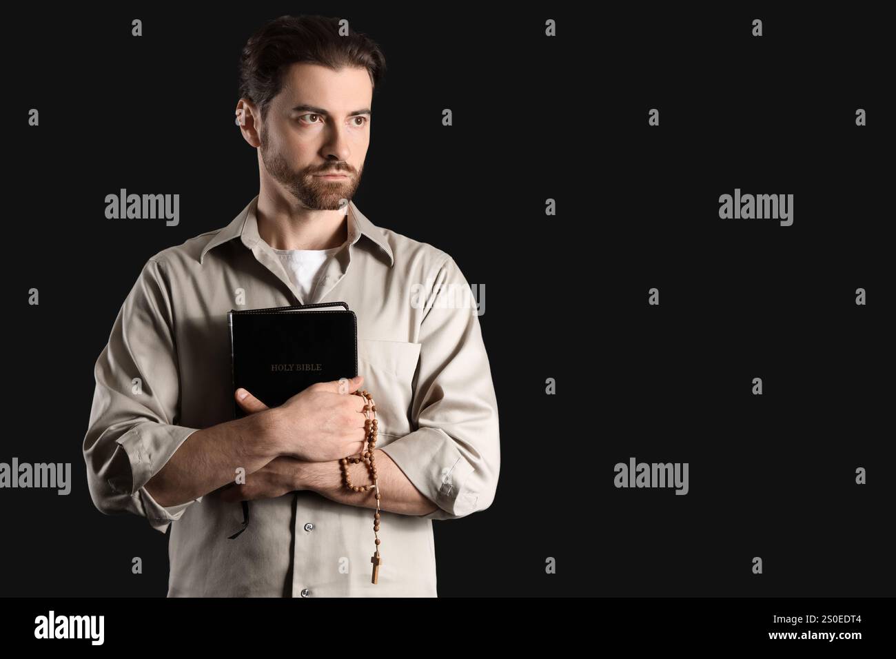 Religious man with Bible and rosary beads on black background Stock ...