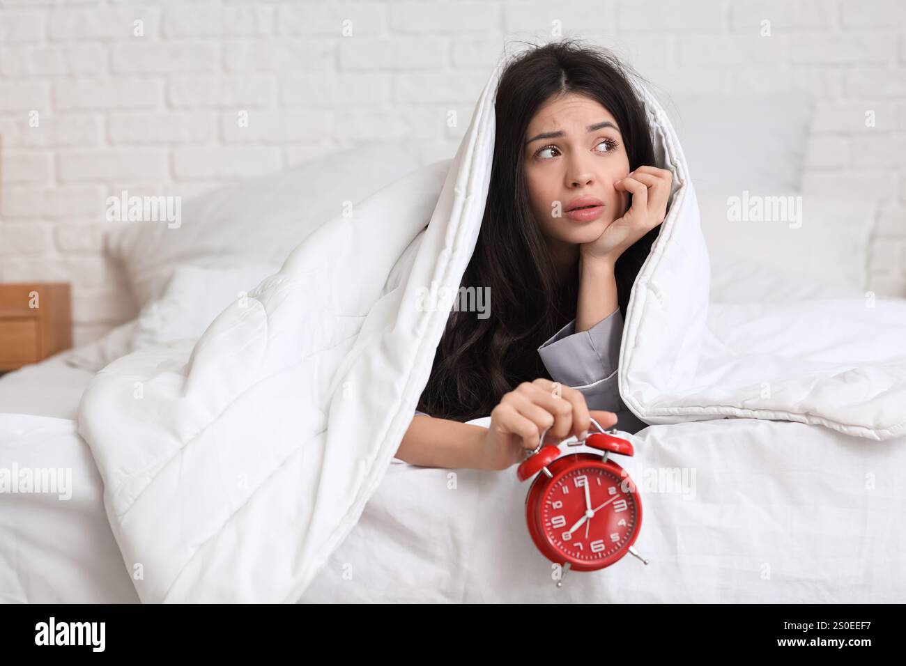 Upset young woman with blanket and alarm clock lying in bedroom Stock ...