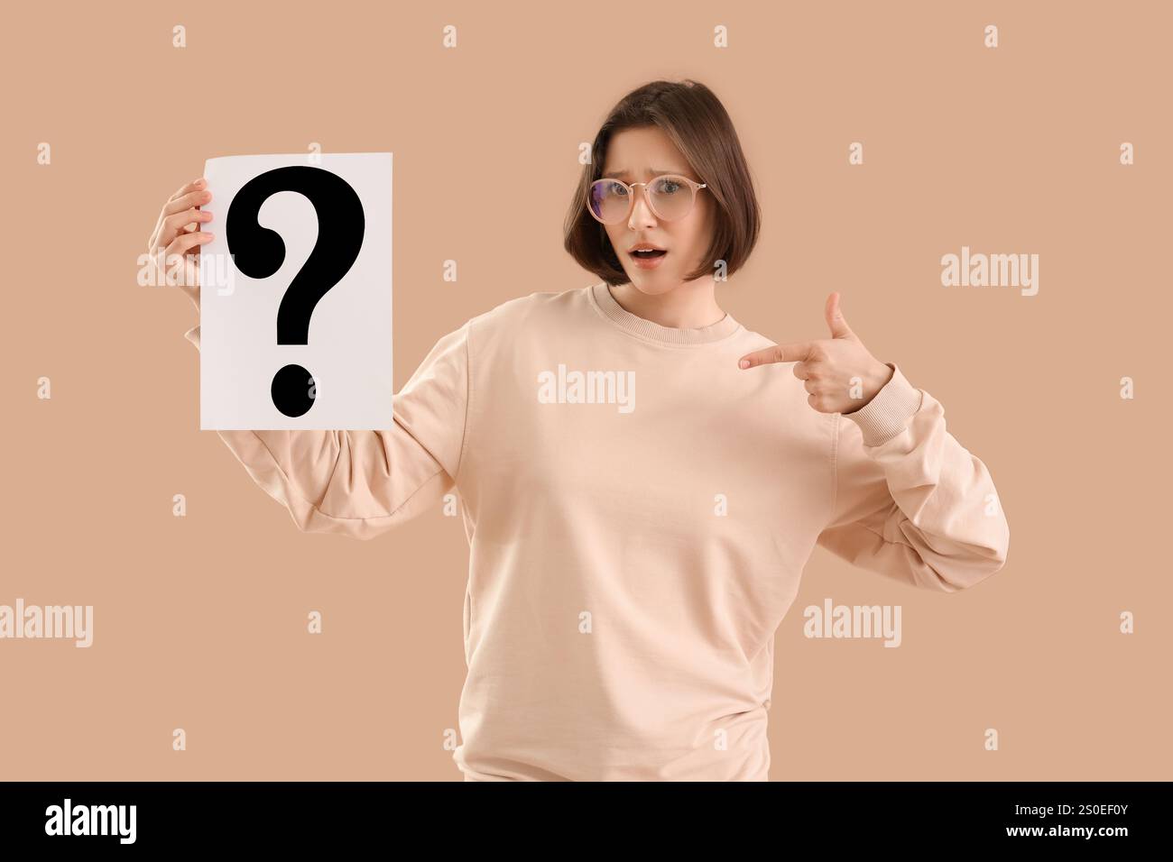 Young woman pointing at paper question mark on beige background Stock ...