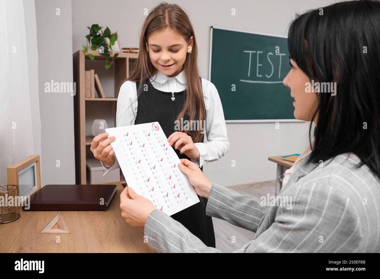 Cute schoolgirl receiving answer sheet with A grade from teacher in ...
