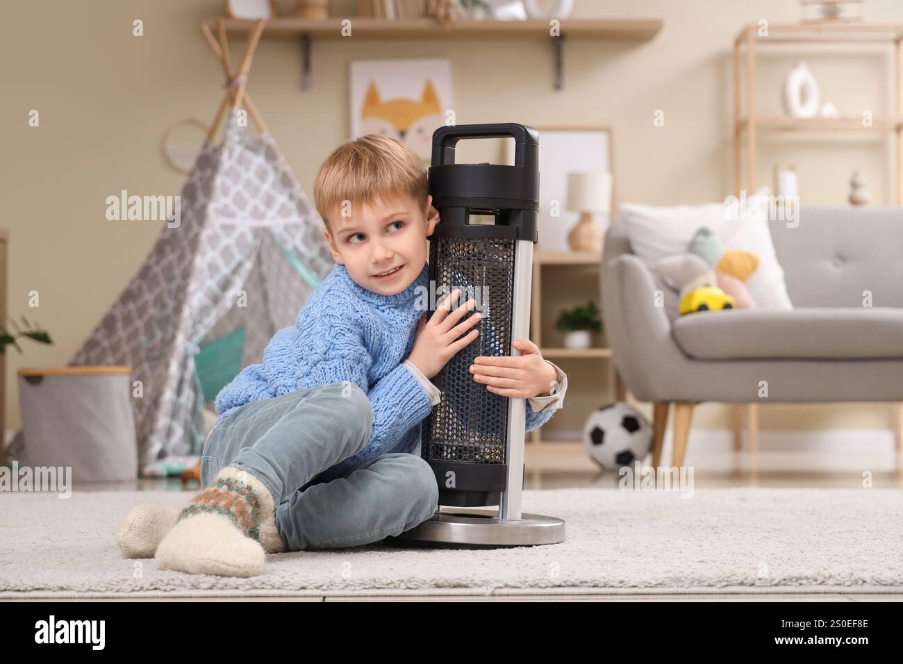Cute little boy hugging electric heater at home Stock Photo - Alamy