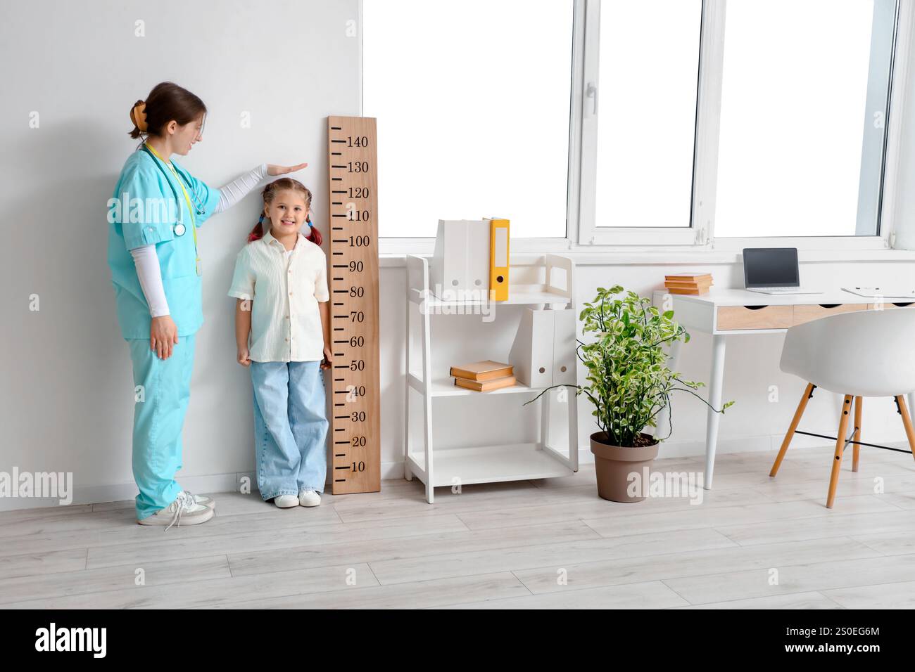 Female pediatrician measuring little girl's height near stadiometer in ...
