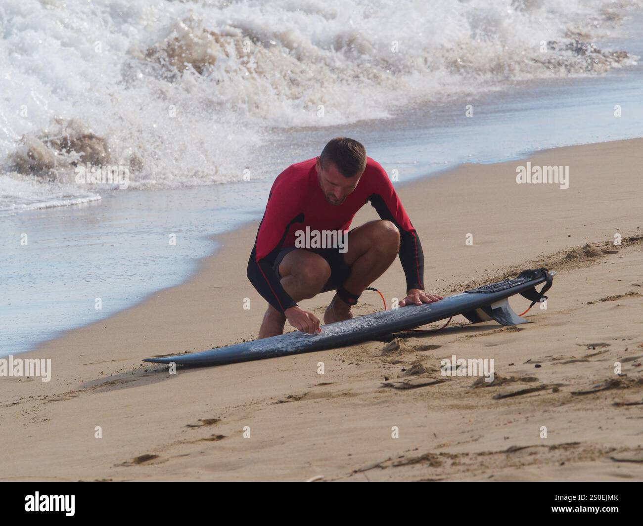 Surfer preparing his board on the beach before heading into the ocean ...