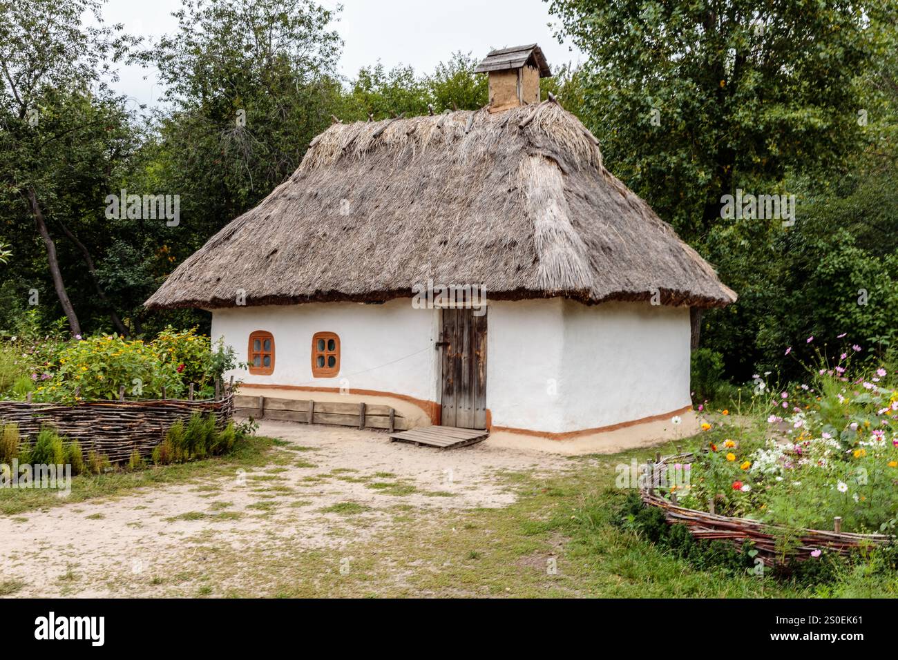 A small, old-fashioned house with a thatched roof sits in a garden. The ...