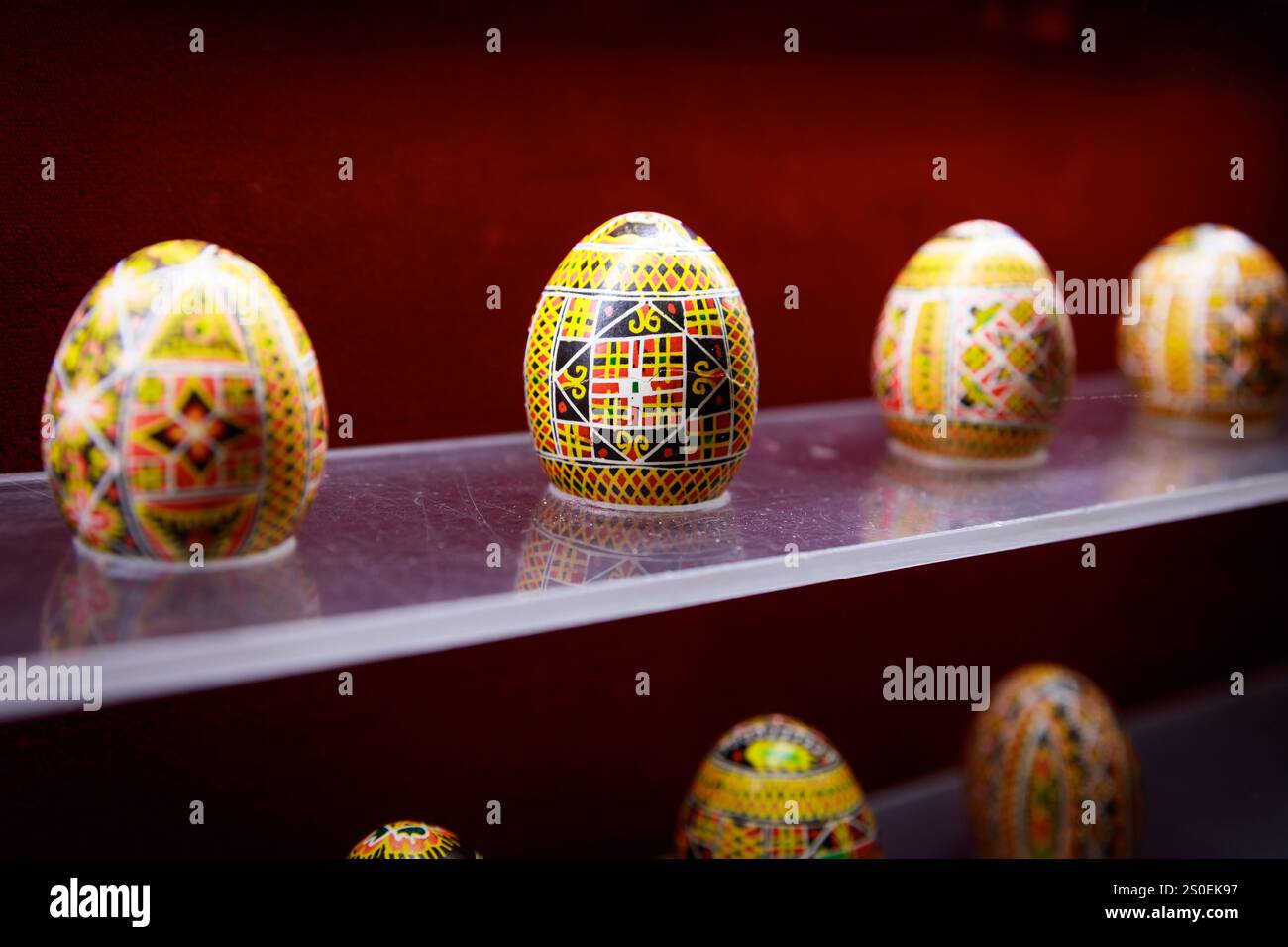 A row of colorful eggs are displayed on a shelf. The eggs are painted ...