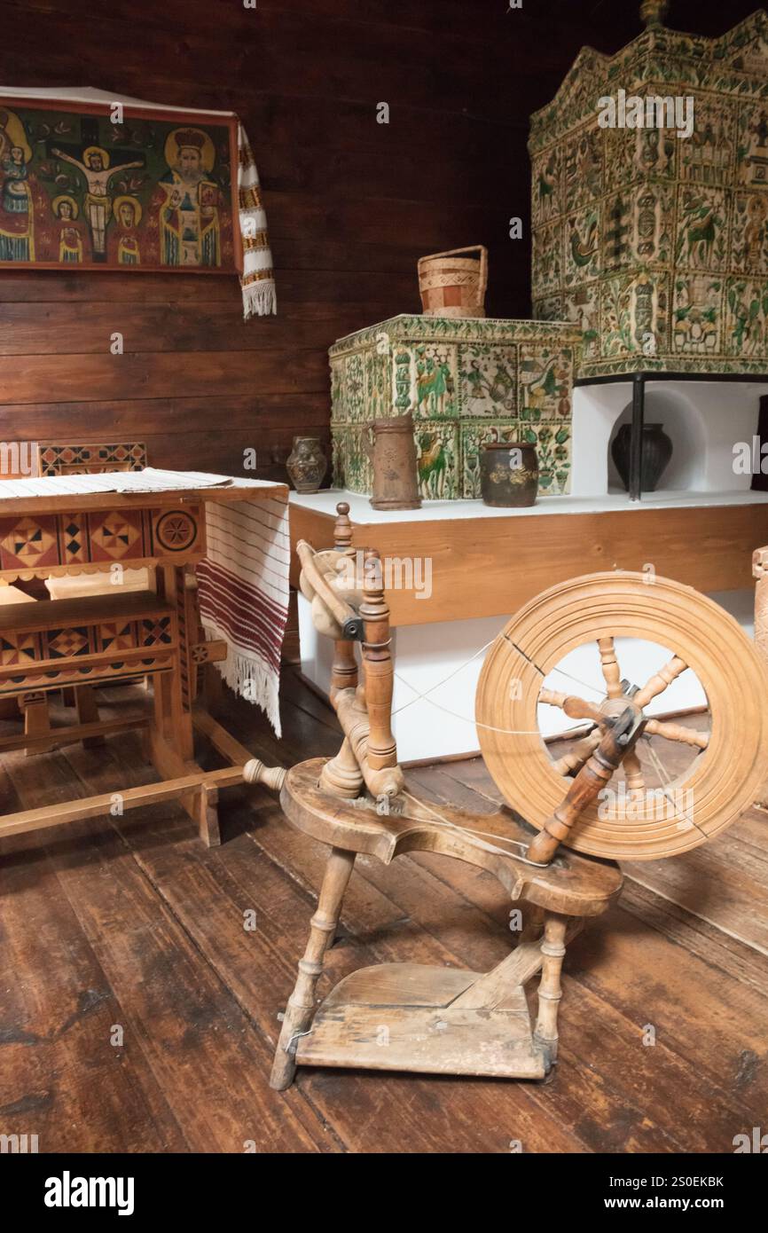 A wooden spinning wheel sits on a wooden table in a room with a stove ...