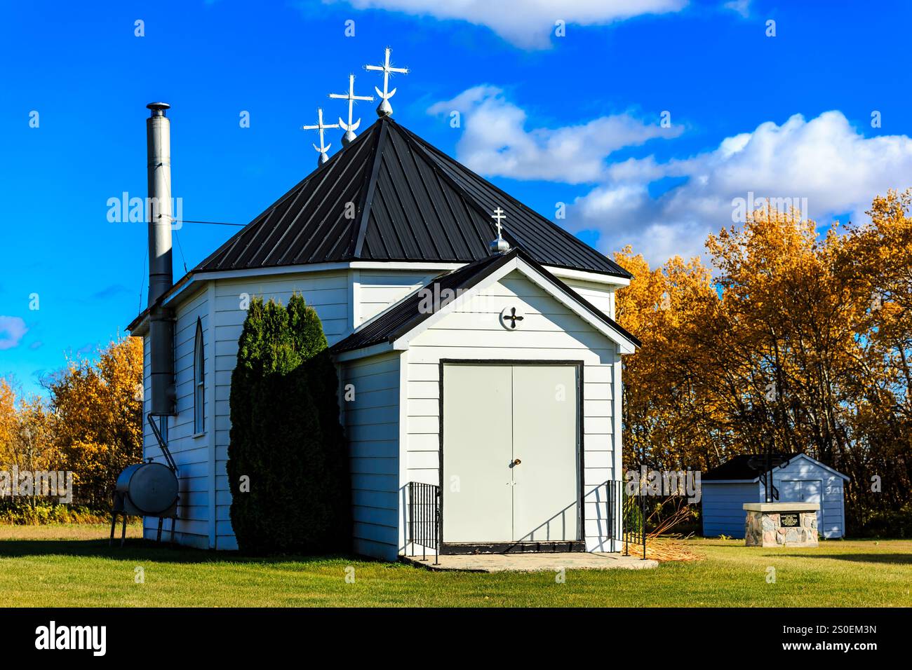 A small white building with a black roof and a cross on top. The ...