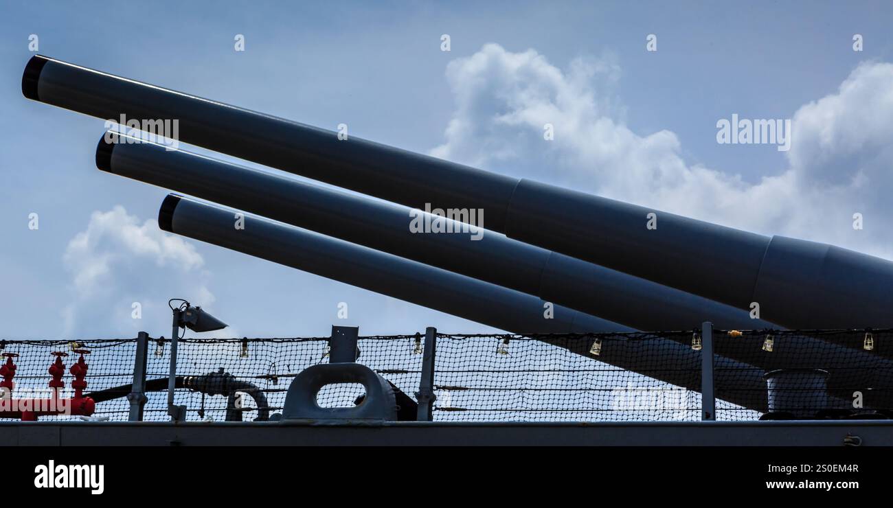 Three large guns are lined up on a ship. The guns are black and the sky ...