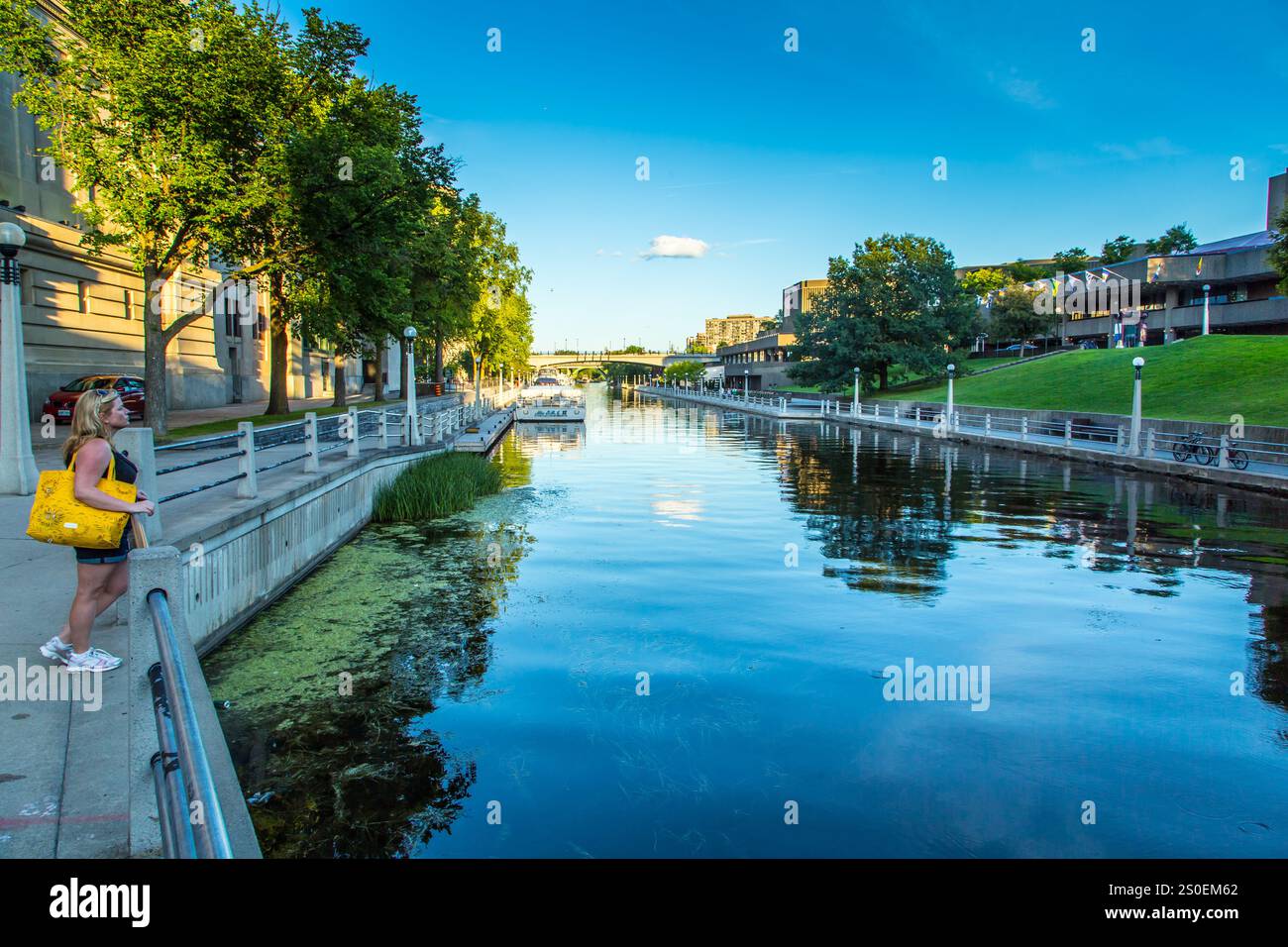 A woman stands on a bridge overlooking a river. The water is calm and ...