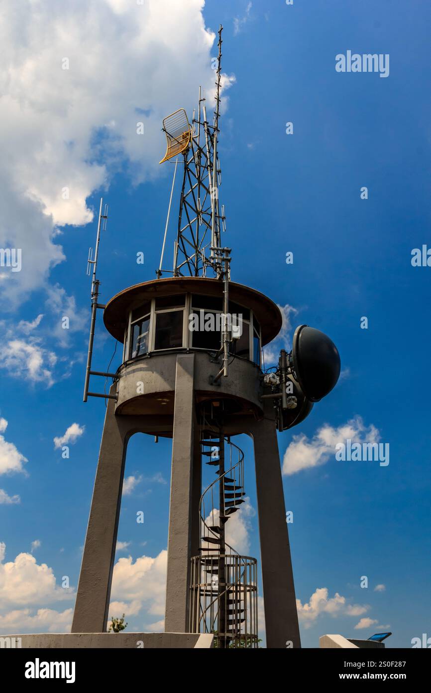 A tall tower with a weather station on top. The sky is blue with some ...