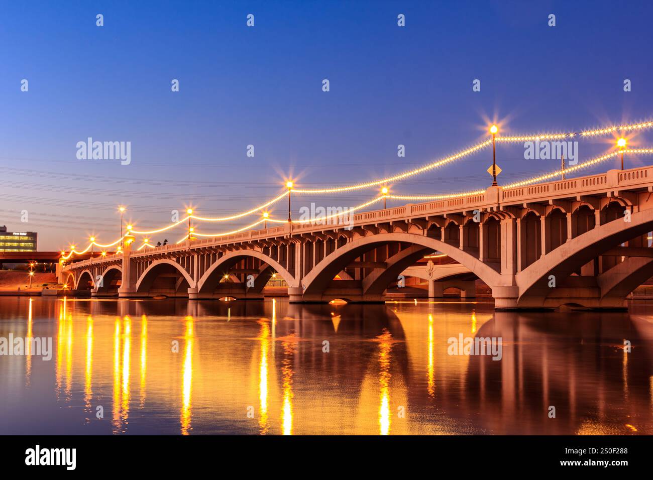 A bridge with lights hanging from it over a river. The lights are lit ...