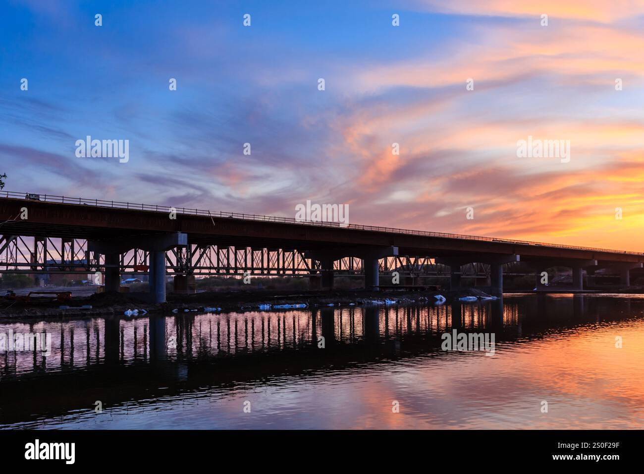 A bridge spans a river with a beautiful sunset in the background. The ...