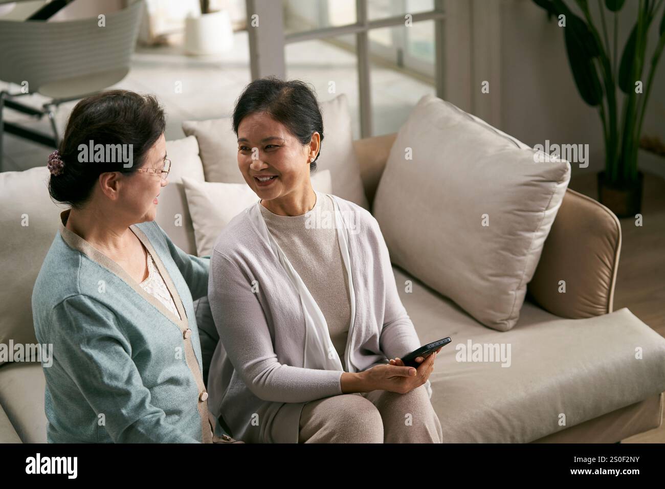 two happy senior asian women sitting on family couch having a pleasant conversation Stock Photo ...