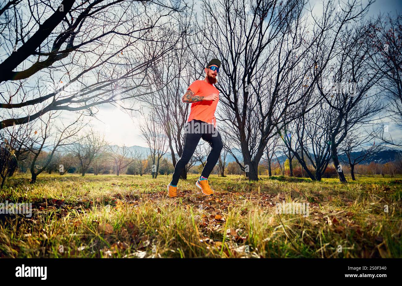 Athletic bearded man in red shirt running on trail path in autumn ...