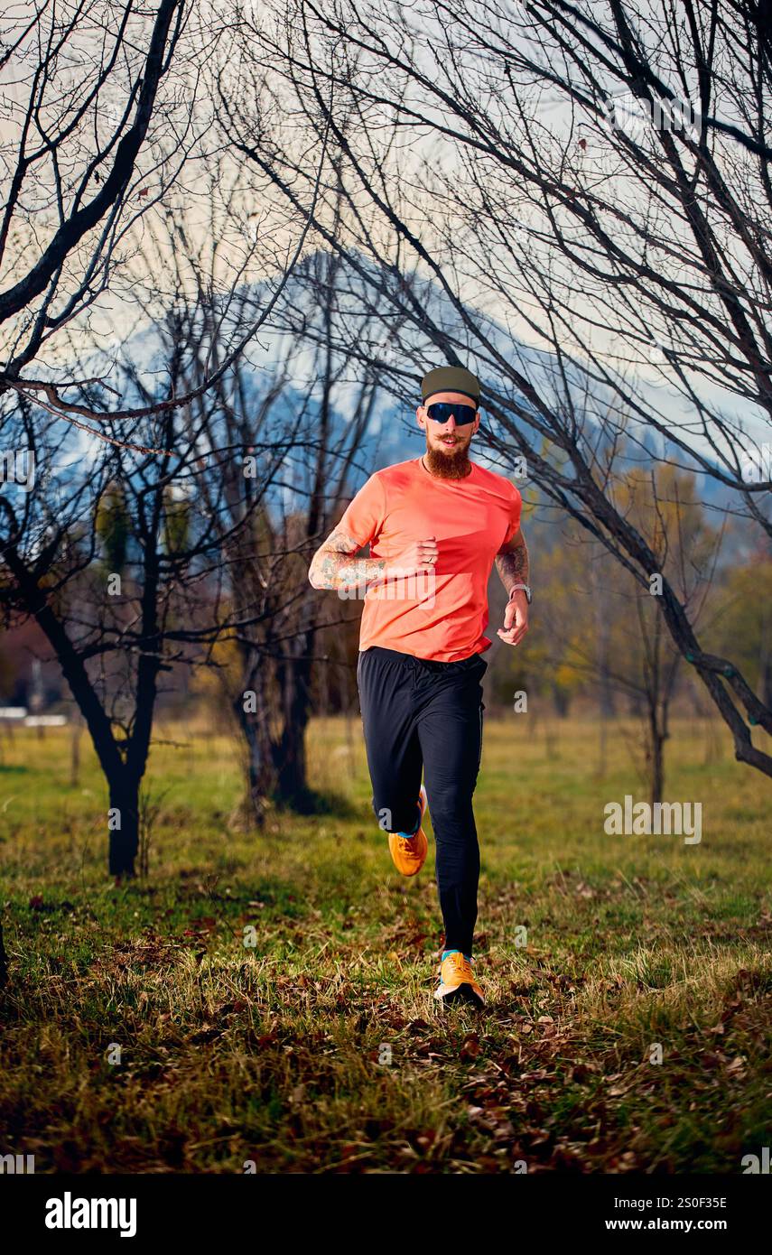 Athletic bearded man in red shirt running on trail path in autumn ...