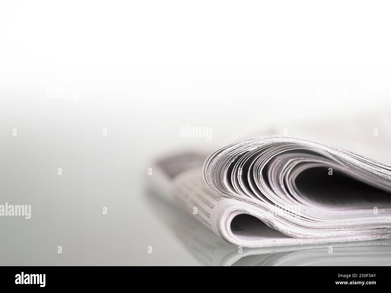 Folded newspapers mirrored on a glass table against a plain light ...