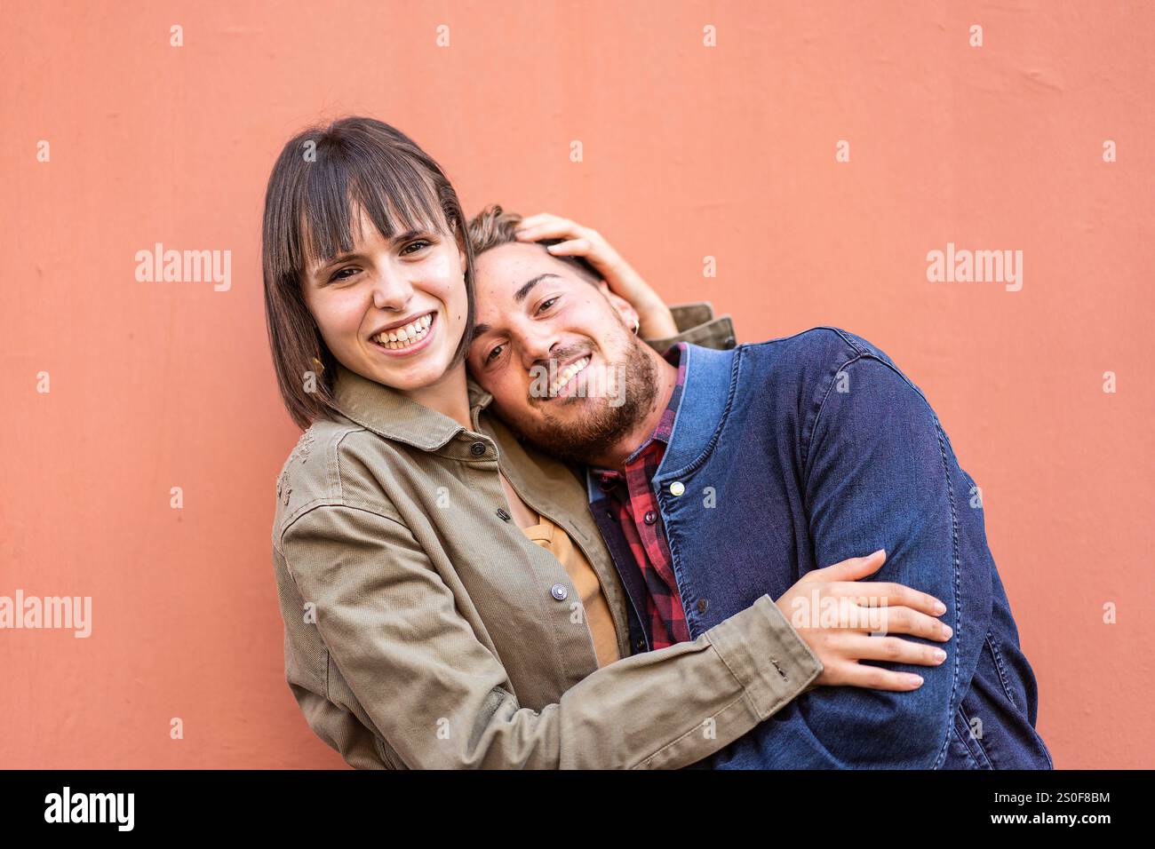 Playful embrace between two young friends smiling against a pastel wall ...