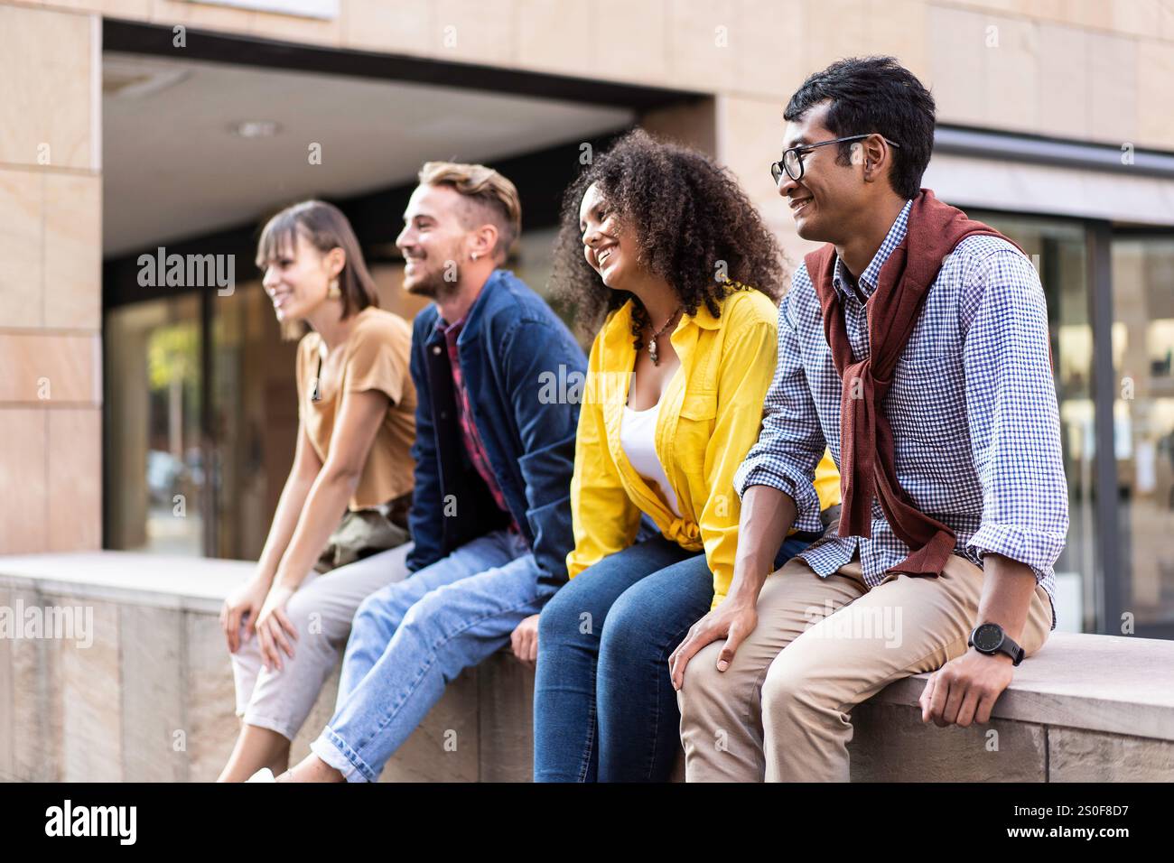 Group of diverse young friends sitting outdoors in an urban setting. A ...