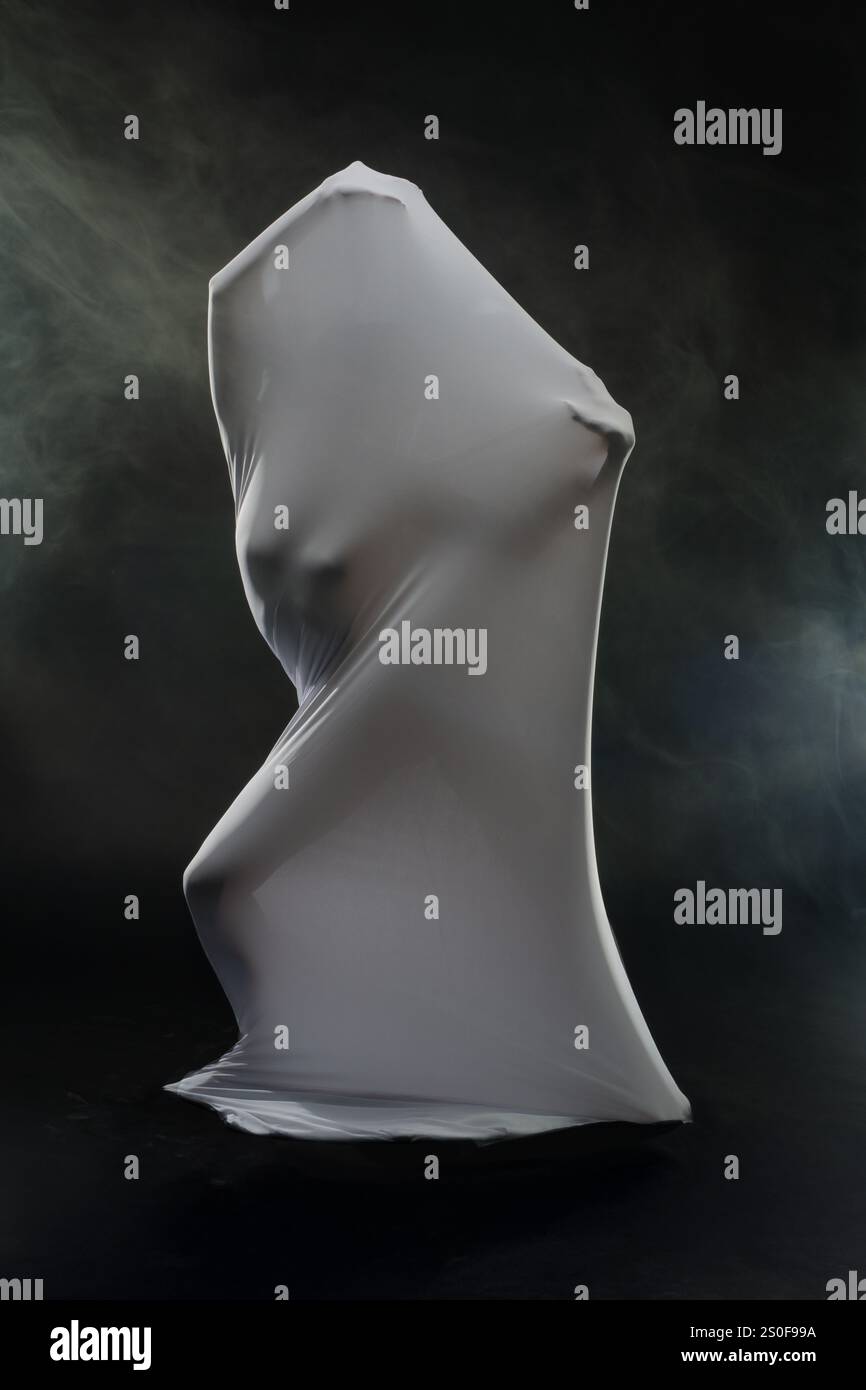Creative sculpture of a human form draped in fabric against a dark ...