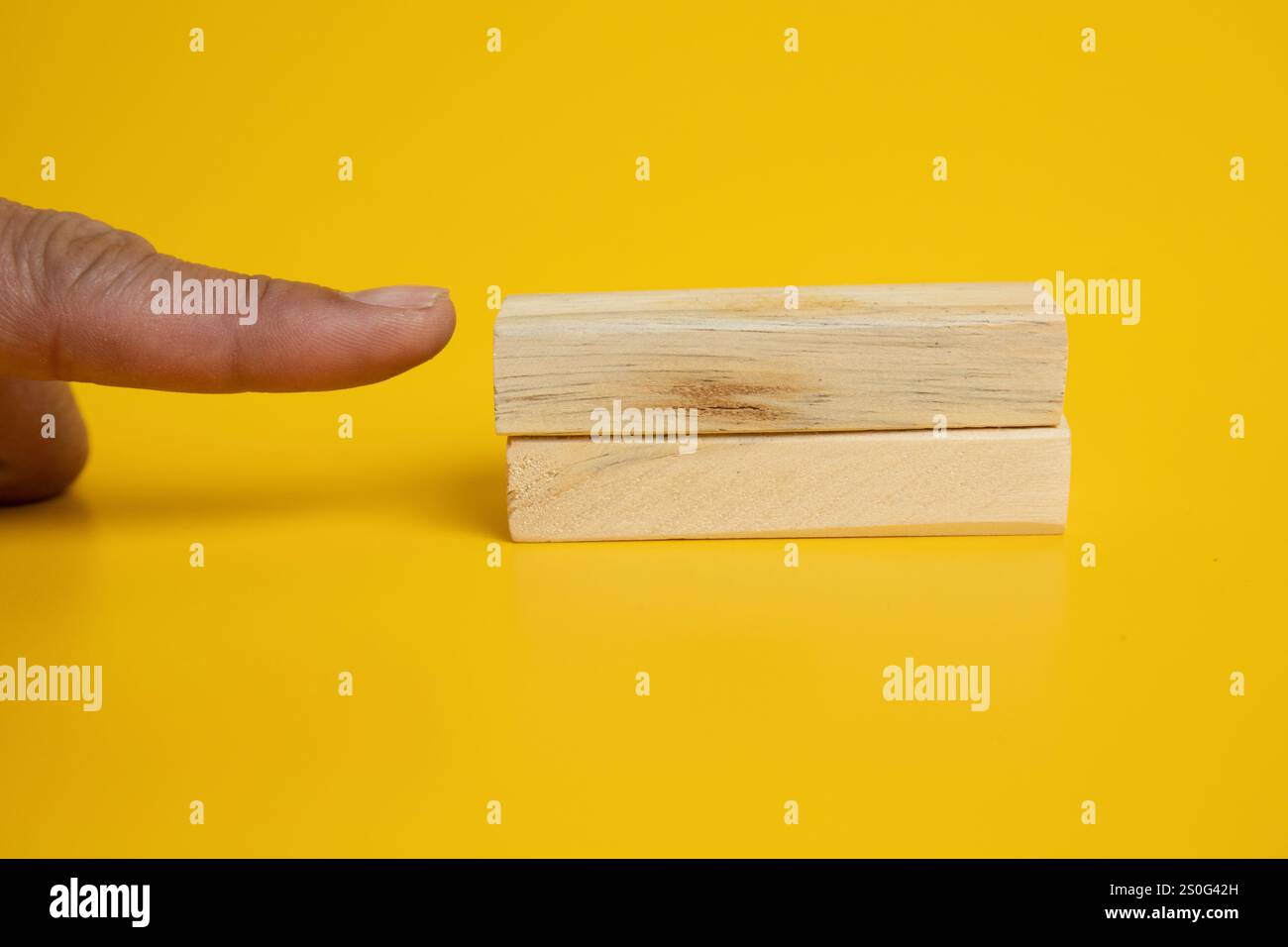 pointing a finger at two jenga blocks arranged neatly on a solid yellow ...