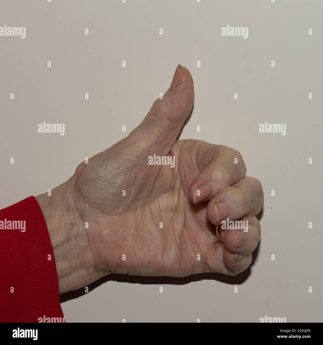 A detailed view of a senior woman's hand showing a thumbs-up gesture ...