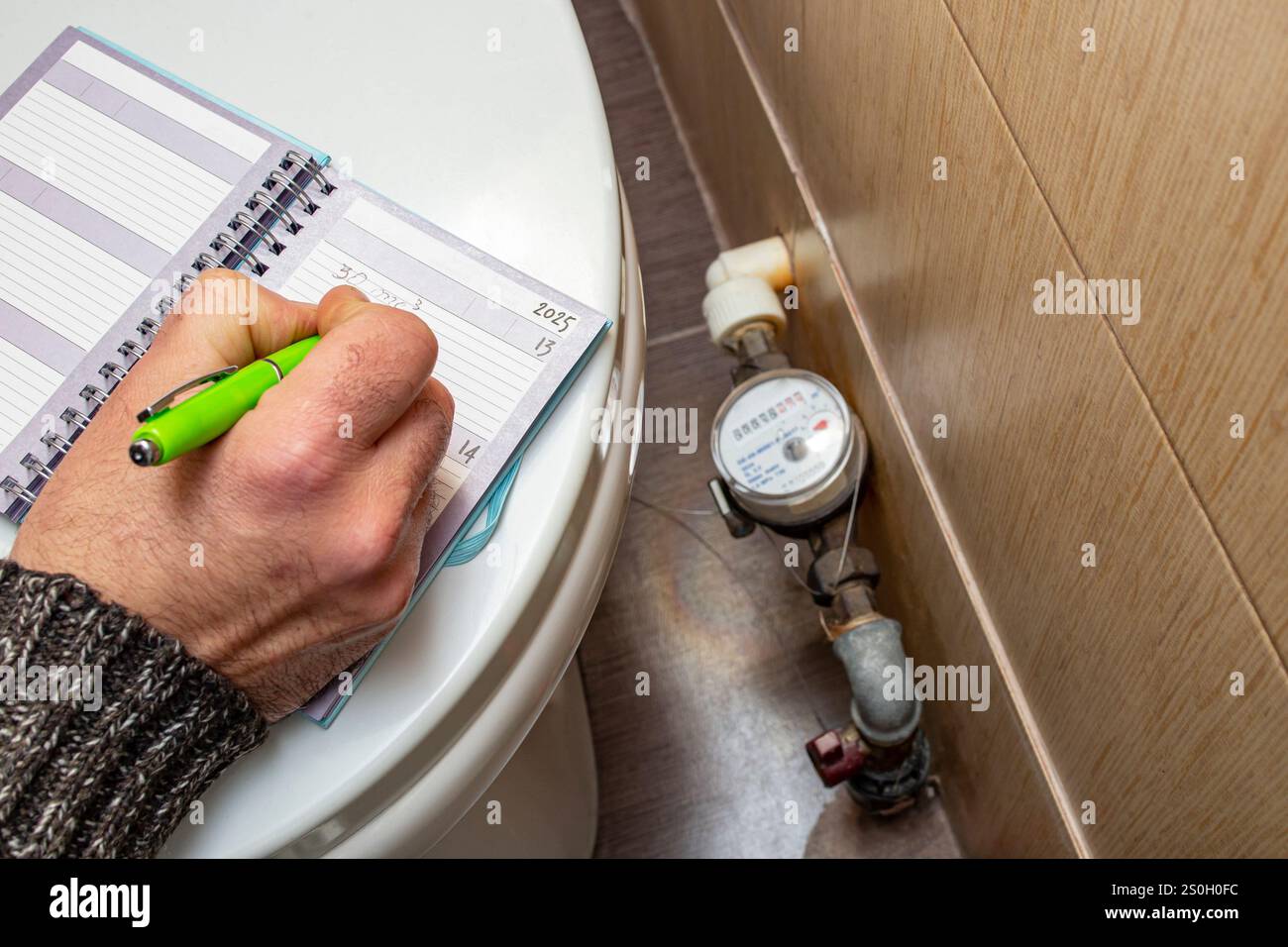 Male hand writing water consumption from a water meter counter inside a ...