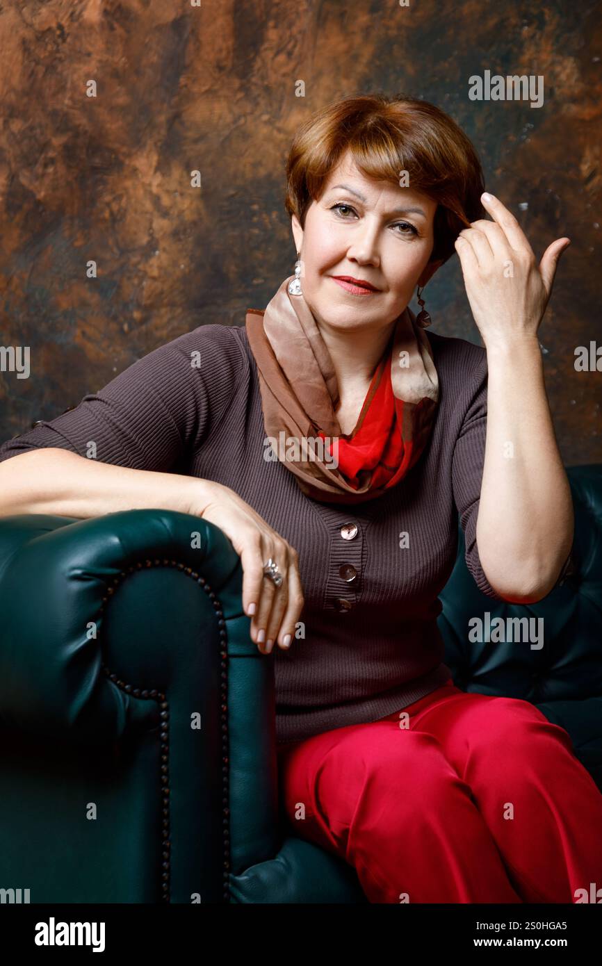 Nice middle aged woman in red pants sitting on a black couch on a brown ...