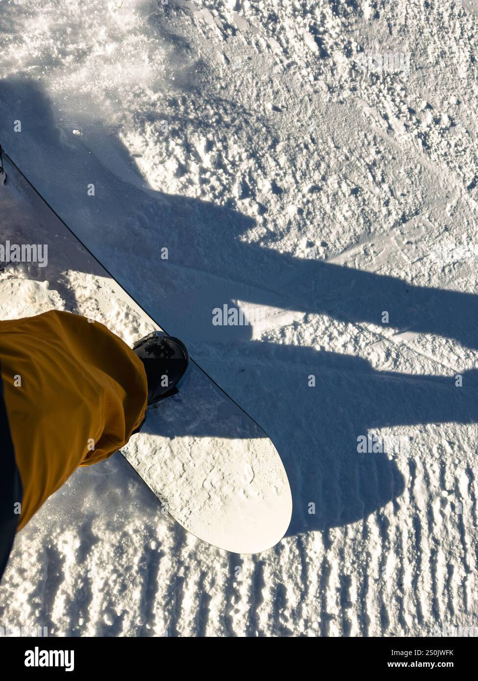 A snowboarder in yellow pants stands on a snowboard, casting a shadow ...