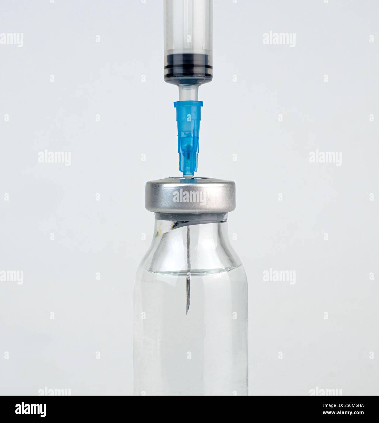A syringe is inserted into a vial, drawing liquid into the syringe for ...