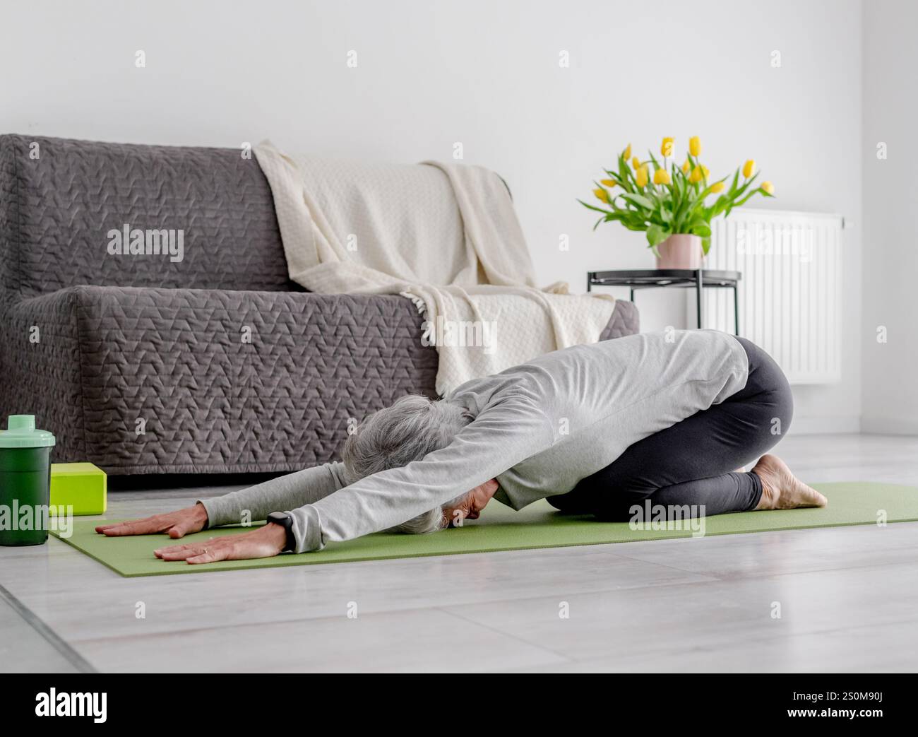 Grey-Haired Woman In baby Pose Practices Yoga At Home On The Floor In A ...