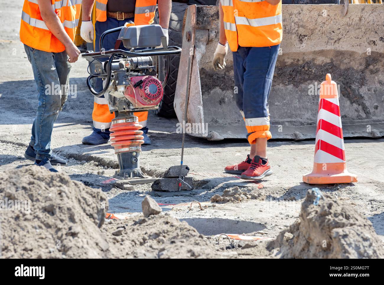 Workers engage in construction activity using a compactor in a busy ...