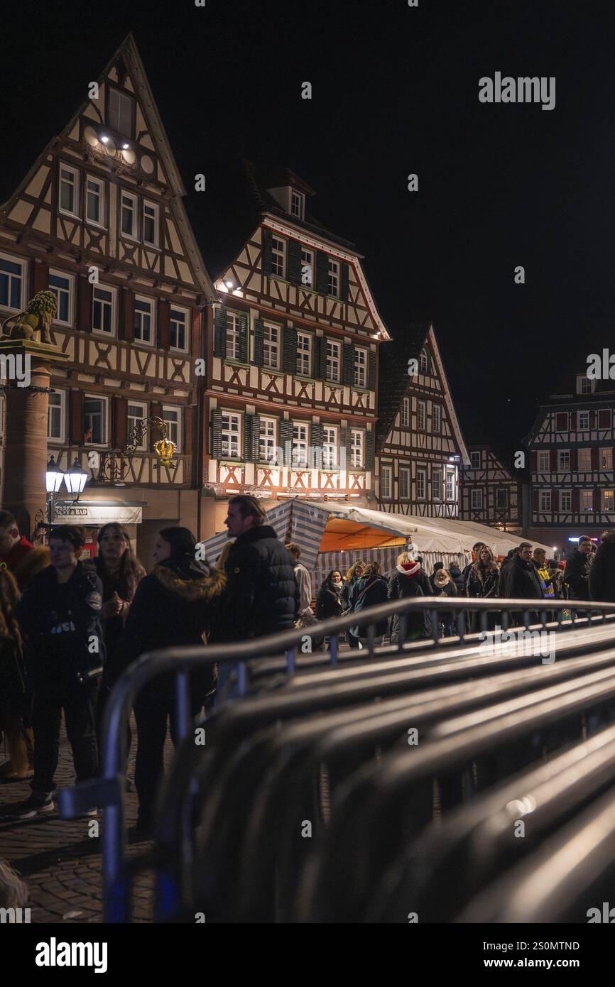 Crowd gathers at night in front of illuminated half-timbered houses and ...