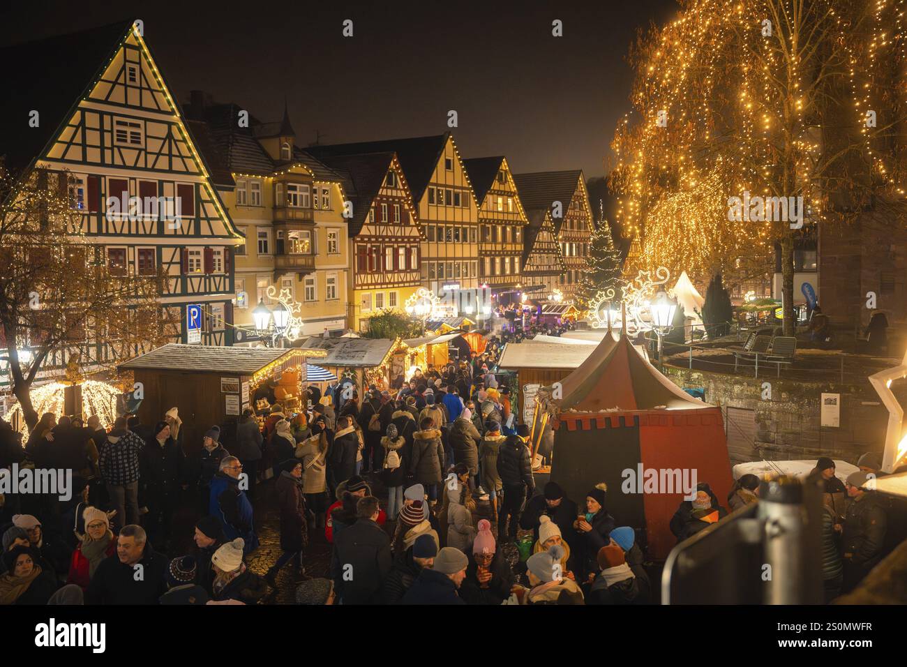 Crowds of people at a Christmas market at night surrounded by festively ...