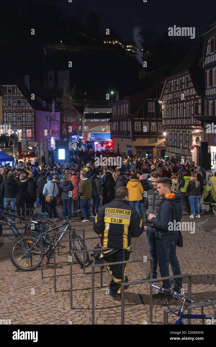 In a town centre, a crowd gathers at night in front of half-timbered ...