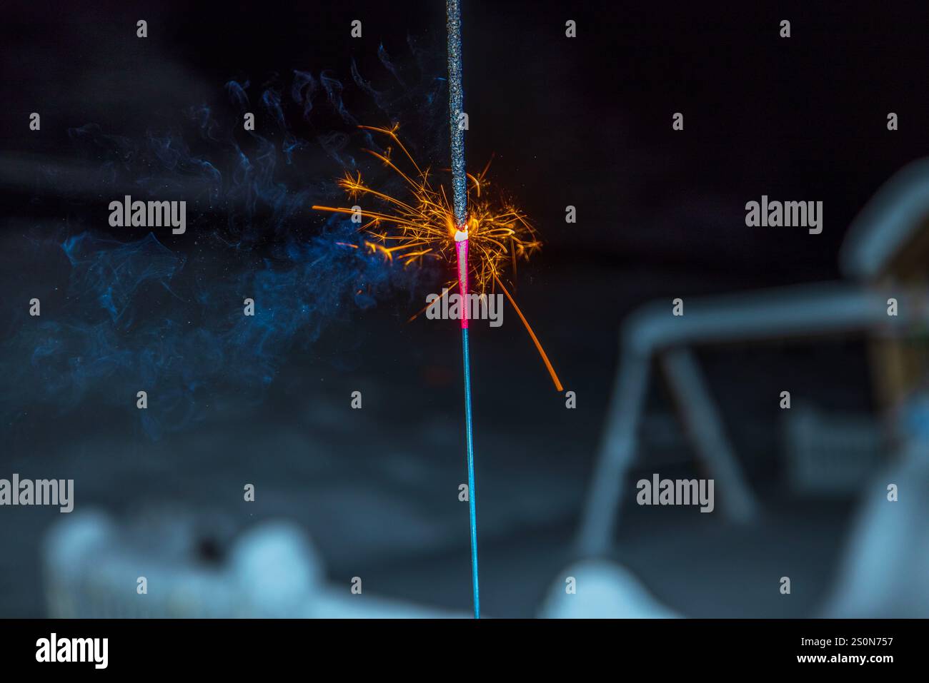Sparkler burning brightly with glowing orange sparks and blue smoke ...