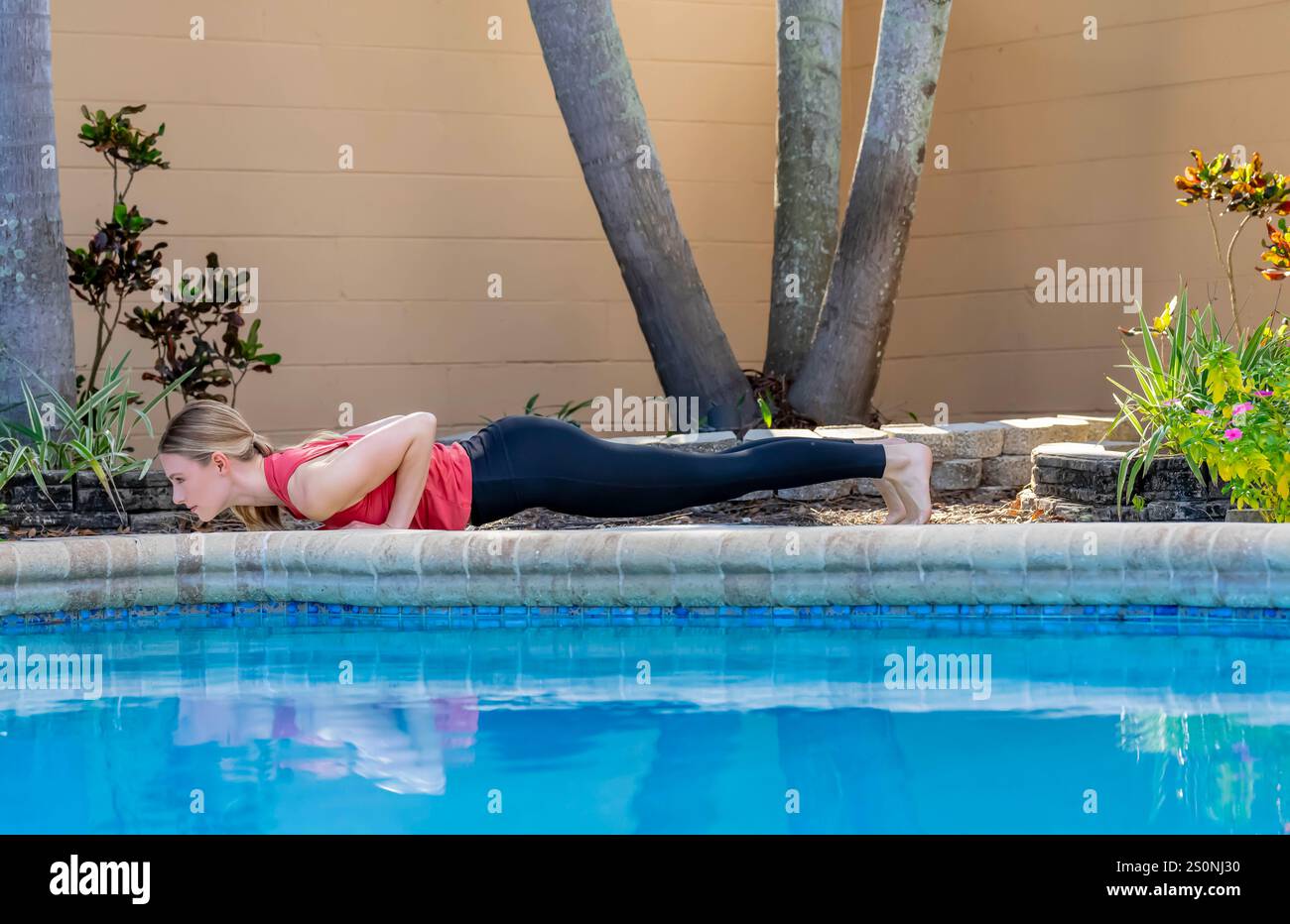 A beautiful young blonde woman practices morning yoga by her pool ...